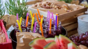 Uma mesa com diversos alimentos, incluindo potes de bebidas com canudos coloridos, uma fatia de melancia e uma tigela de uvas.