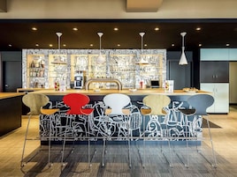 Uma área de bar moderna com design de arte única na parede, um balcão com máquina de café e um espaço de estar com um banco estampado.