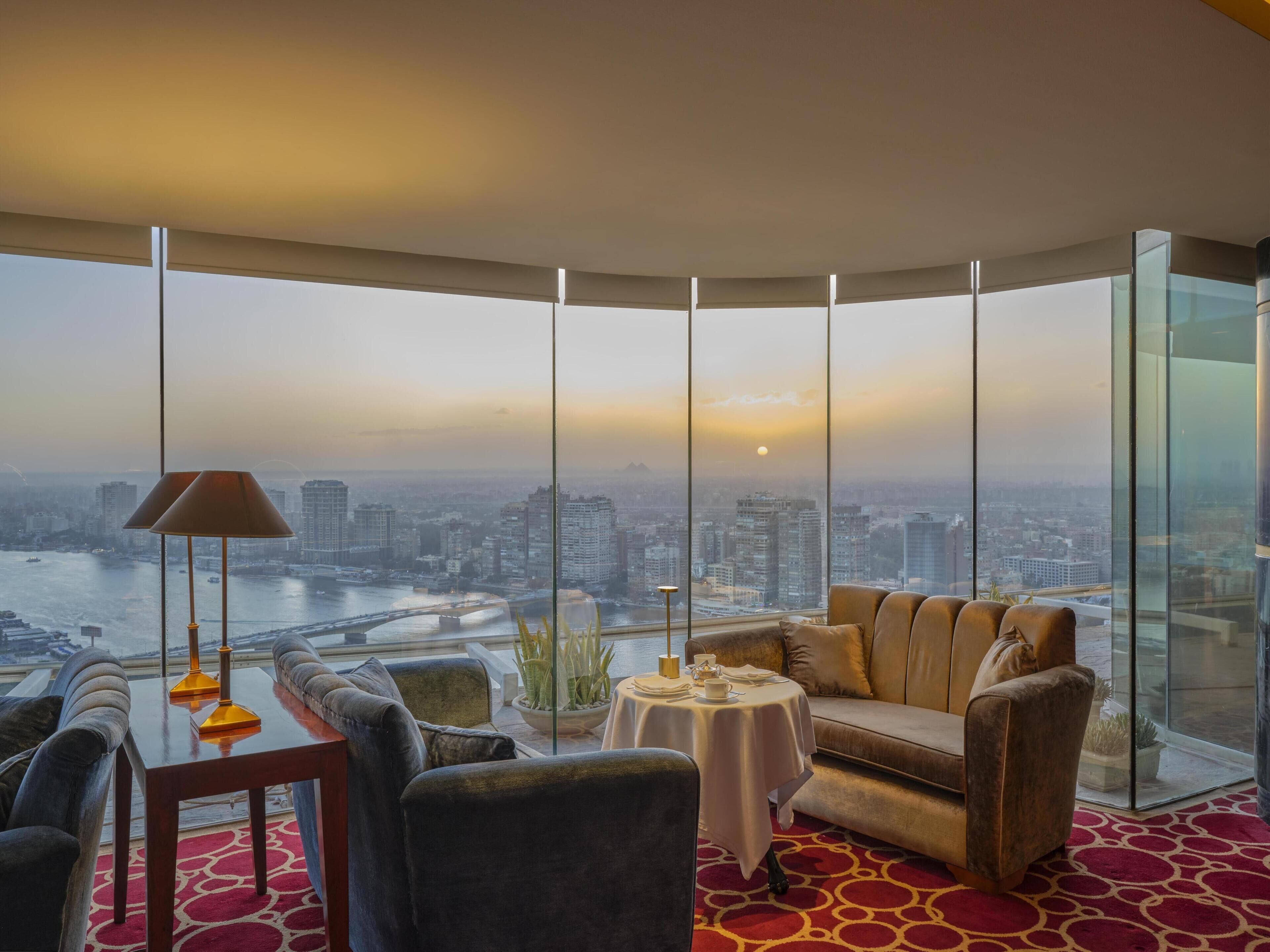 Quarto em edifício alto com vista para a cidade, um sofá, uma mesa e um abajur.