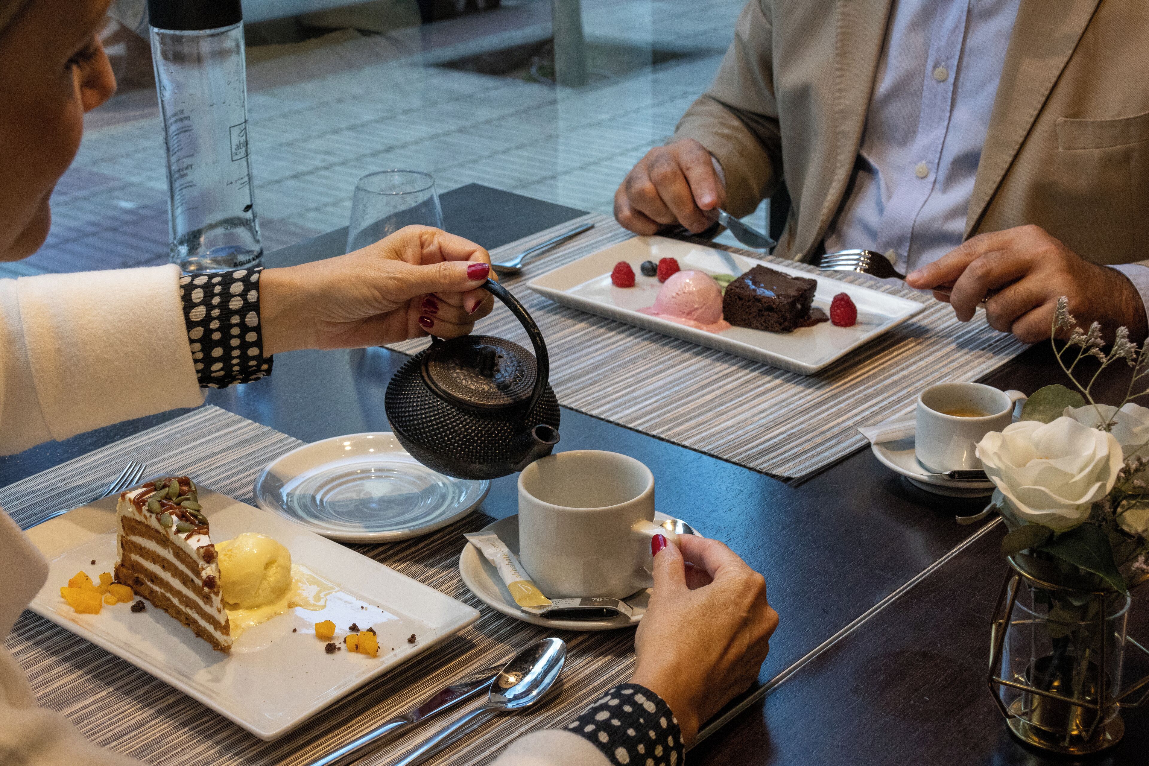 Uma mesa de jantar com um prato de comida, uma chávena de café e um bule de chá.