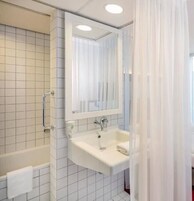 Um banheiro com parede revestida de azulejos brancos, banheira, pia com espelho acima e cortina de chuveiro.