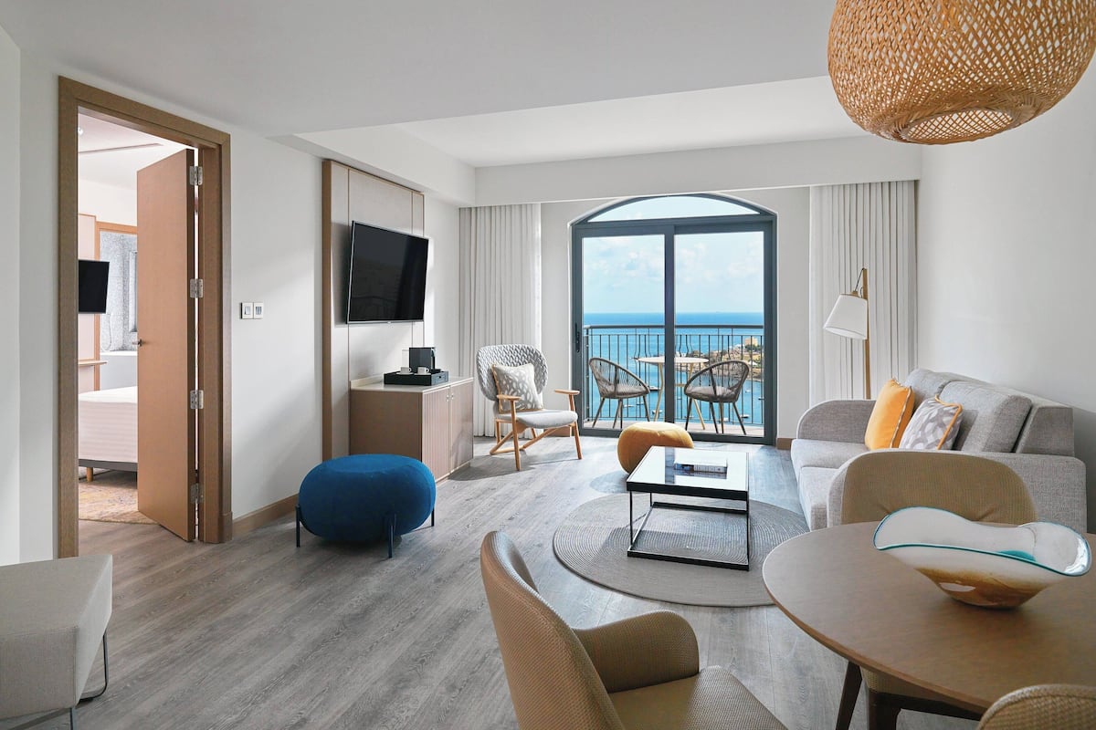 Quarto de hotel moderno com varanda, sofá, mesa de centro e televisão.