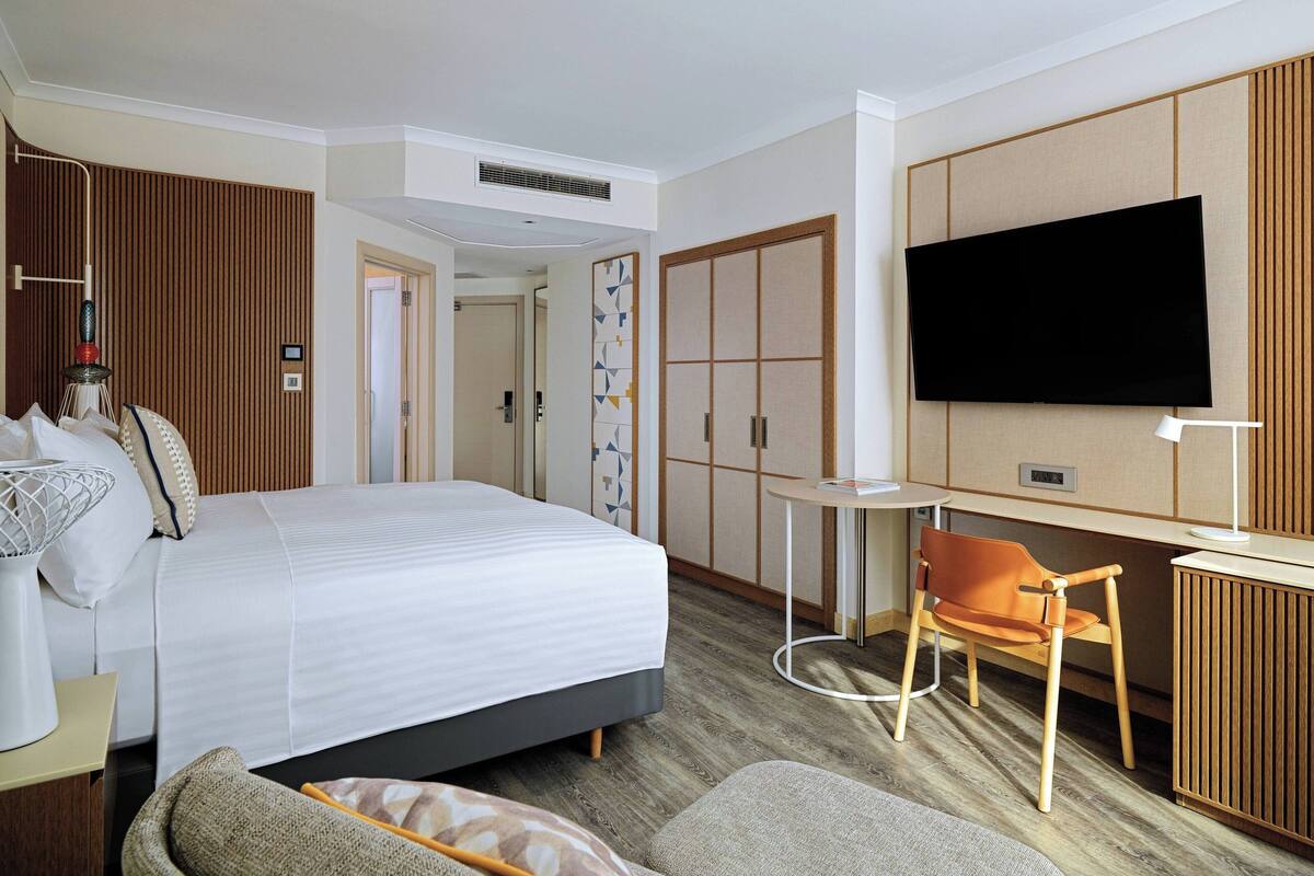 Quarto de hotel com uma cama, escrivaninha, cadeira, televisão e guarda-roupa.