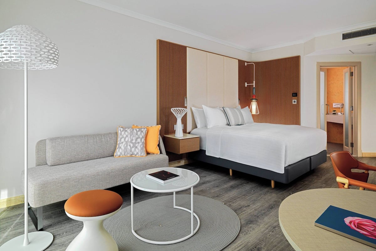 Quarto de hotel moderno com uma cama, um sofá, uma mesinha redonda e uma cadeira.