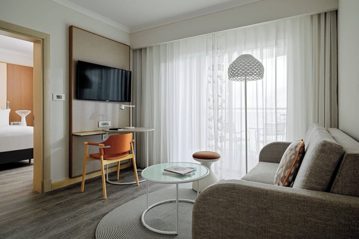 Quarto de hotel moderno com cama, televisão, secretária, cadeira, sofá e mesa redonda.