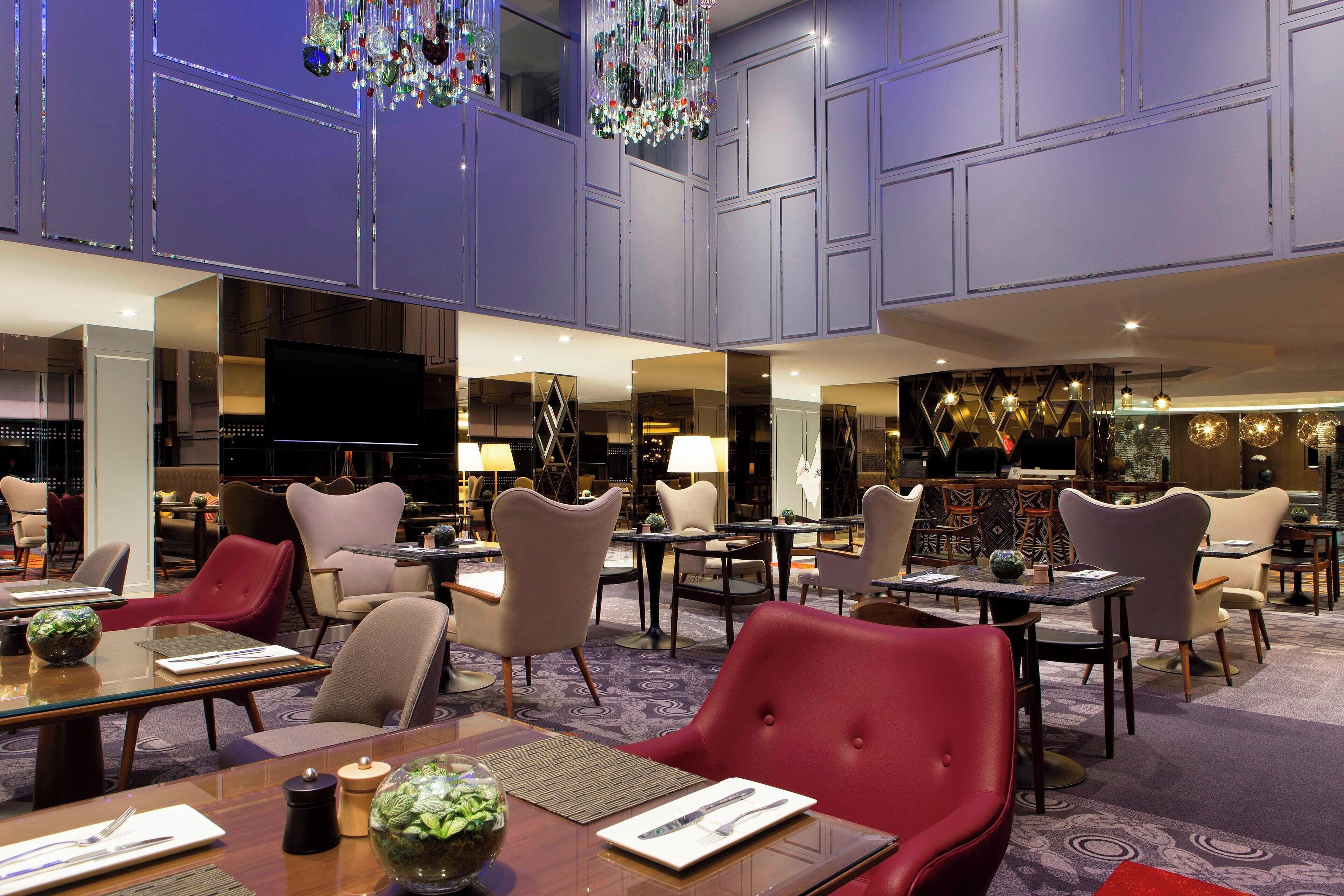Um amplo hall de hotel com diversas áreas de refeições, assentos confortáveis e um lustre moderno.