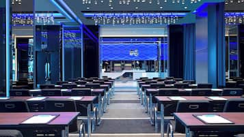 Uma sala de conferências moderna com fileiras de mesas e cadeiras, uma mesa de recepção e teto iluminado em azul.