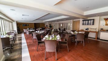 Uma ampla sala de jantar com várias mesas e cadeiras, piso de madeira e design de teto moderno.
