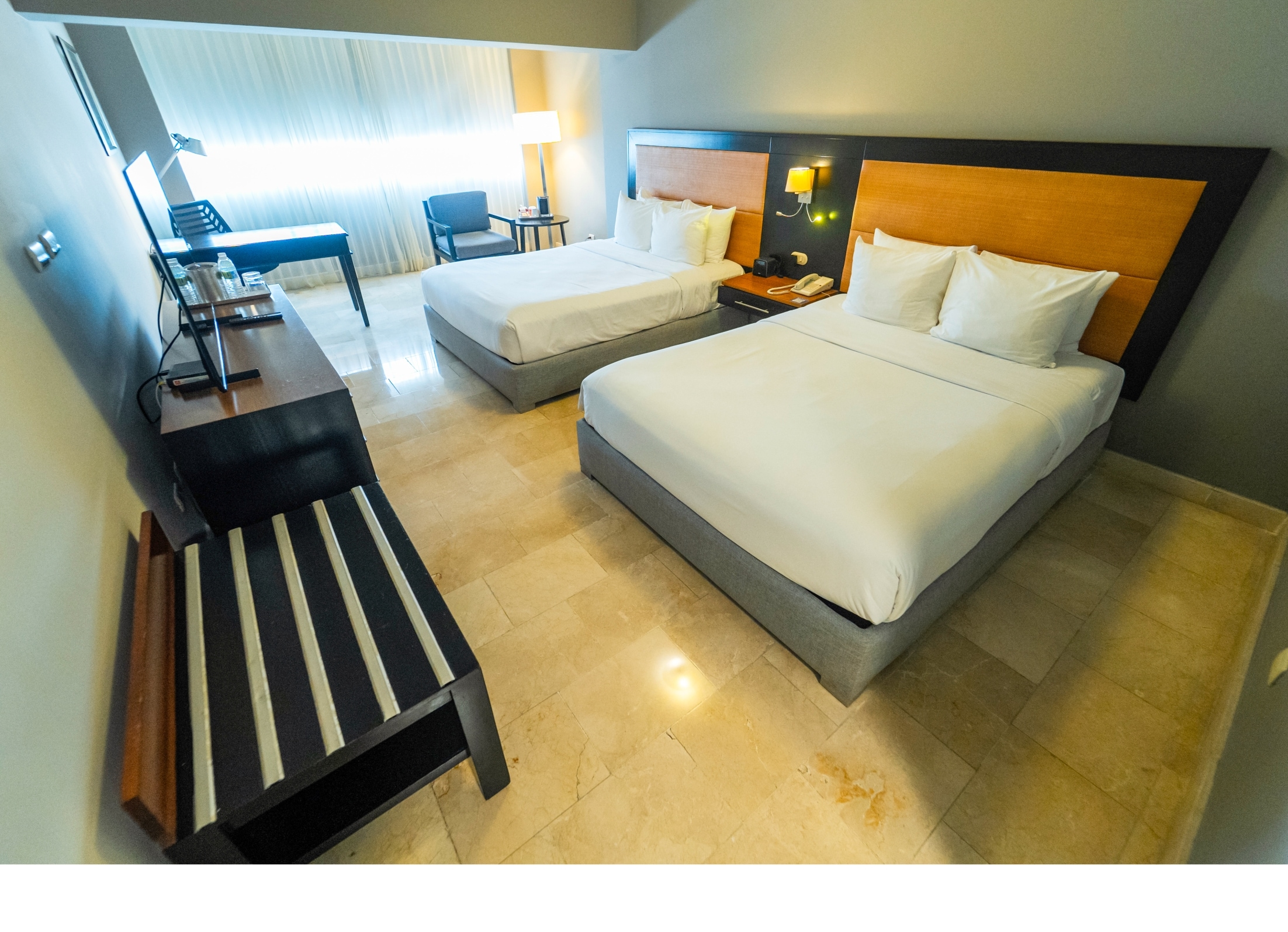 Quarto de hotel com duas camas, uma escrivaninha e uma cadeira.