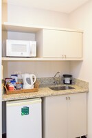 Uma cozinha compacta equipada com micro-ondas, chaleira e um pequeno frigorífico.