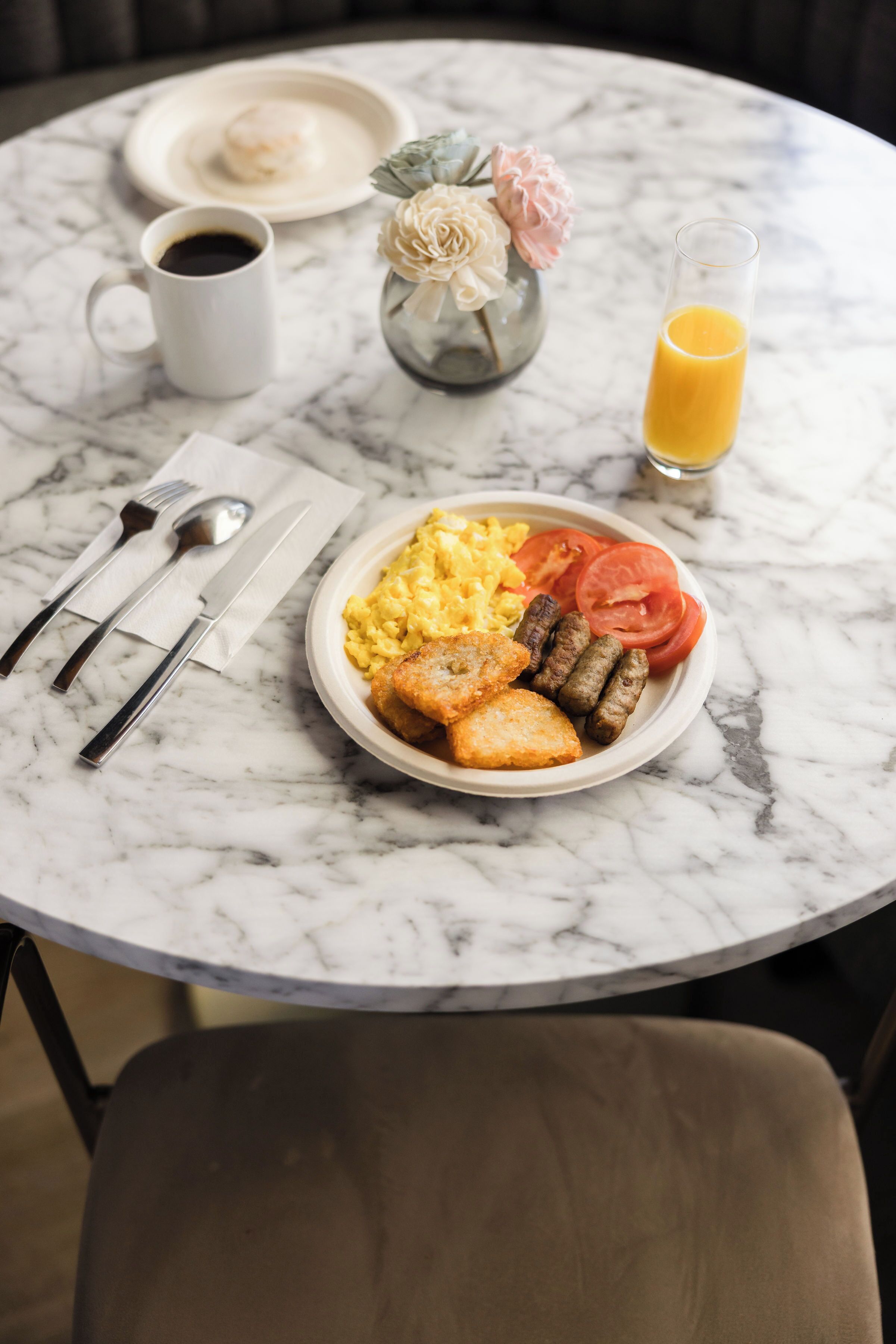 Uma mesa de mármore com um prato de ovos, salsichas, tomates e torradas.