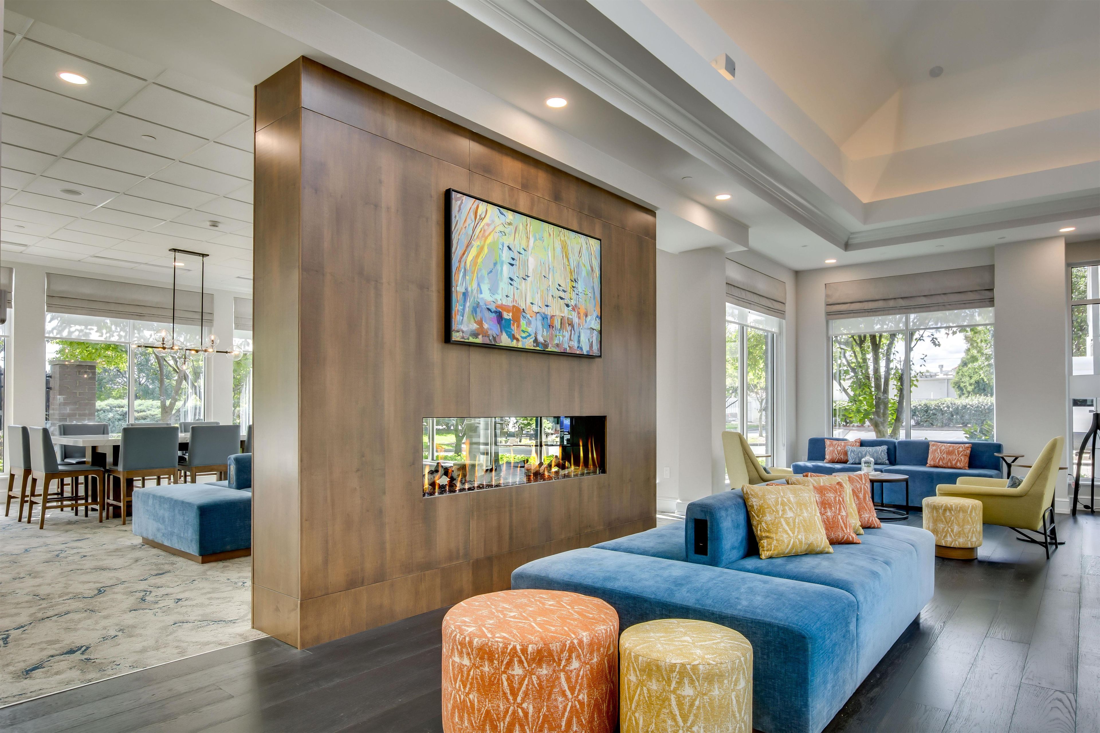 Uma sala de estar moderna com lareira, um grande quadro abstrato e um sofá azul com pufes estampados.