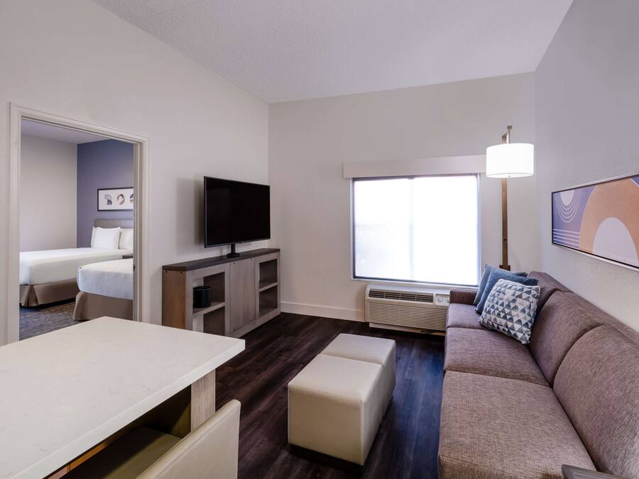Quarto de hotel moderno com sofá, televisão, mesa de jantar e janela com vista.