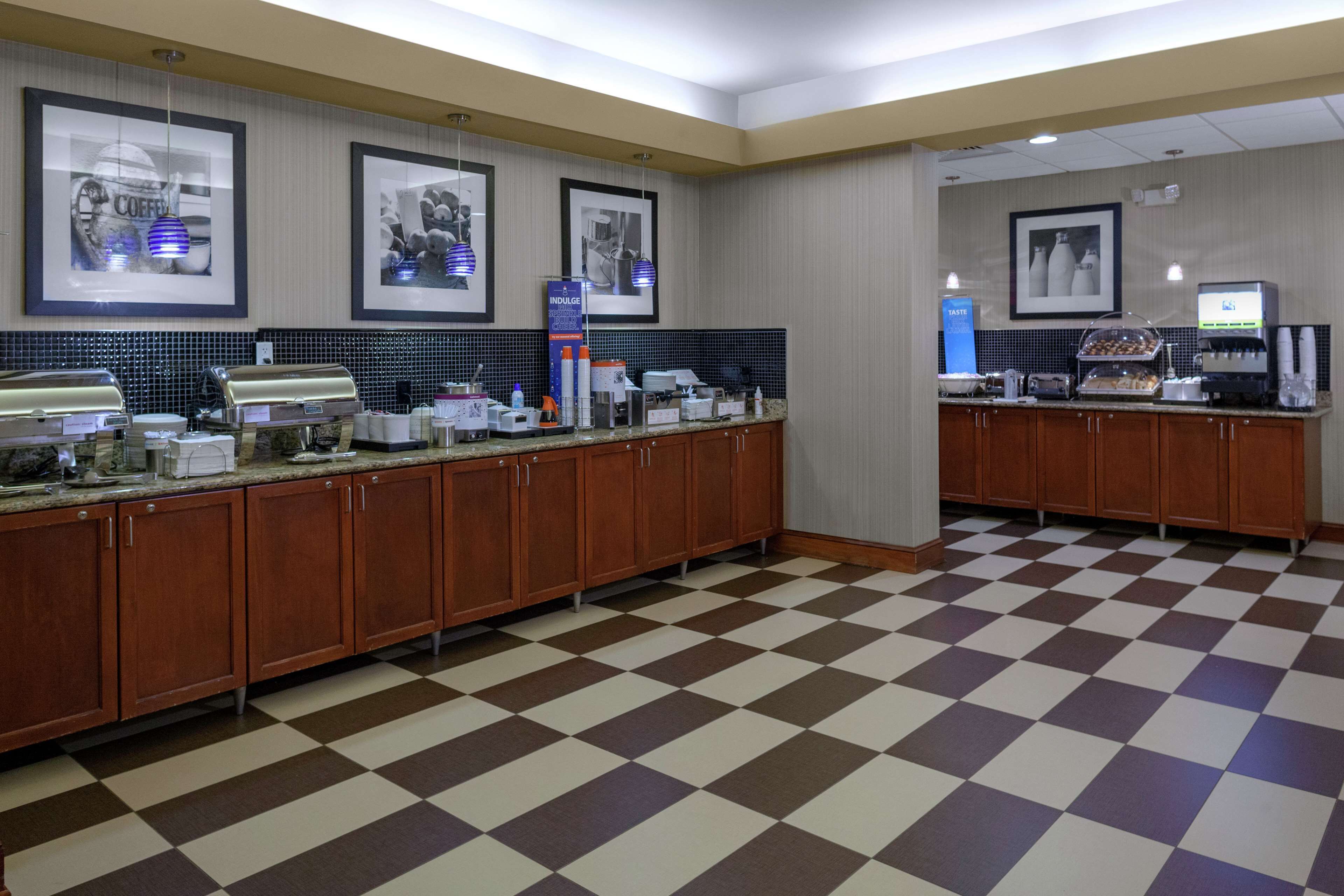 Uma cozinha de hotel com piso xadrez, armários de madeira e diversos eletrodomésticos.