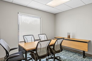 Uma sala de conferência com uma mesa comprida, quatro cadeiras, um quadro branco e uma janela com persianas.