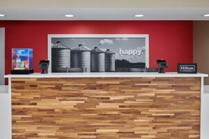 Balcão de recepção com design em painel de madeira, um grande letreiro com a palavra 'happy' e dois dispositivos pretos no balcão.