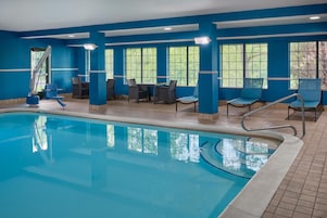 Piscina com paredes e janelas azuis, rodeada por cadeiras e mesas.