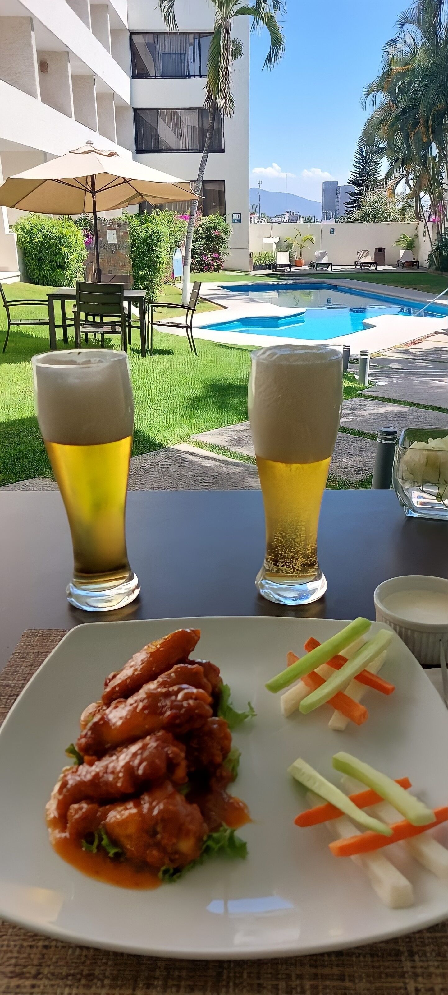 Uma mesa de jantar com dois copos de cerveja, um prato de asas de frango e palitos de legumes.