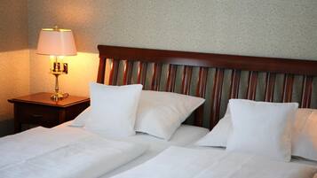 Quarto de hotel com cabeceira de madeira, duas camas com roupa de cama branca e mesa de cabeceira com abajur.