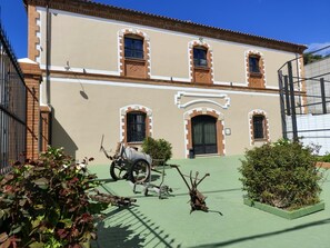 Um edifício de dois andares com fachada bege, várias janelas e telhado verde.