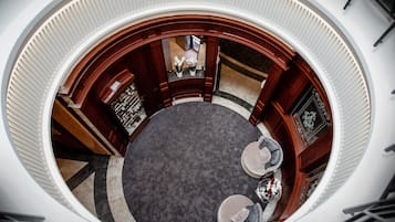 Vista circular de um hall com uma mesa redonda e cadeiras, painéis de madeira e um balcão de recepção.