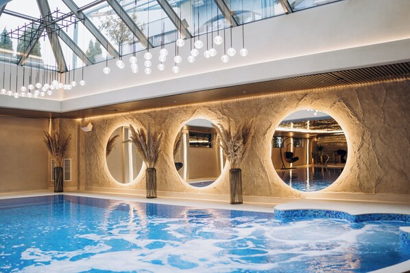 Piscina interna com teto de vidro, janelas circulares e design de teto em madeira.