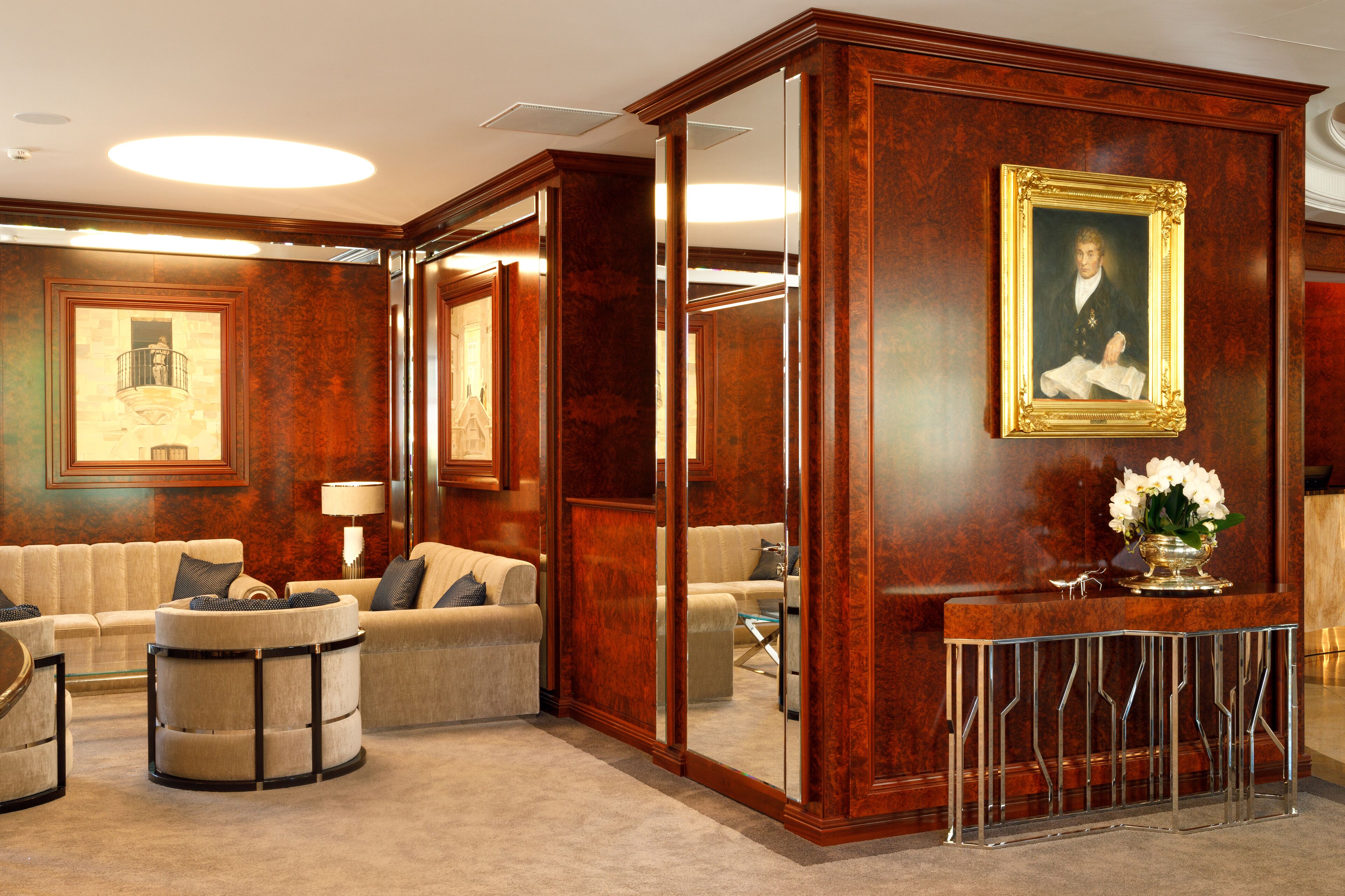 Um hall de entrada luxuoso com teto alto, painéis de madeira elegantes, um espelho grande e um retrato emoldurado.