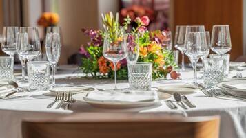 Uma mesa posta para uma experiência gastronômica requintada, com copos, pratos e talheres cristalinos, adornada por um arranjo floral.