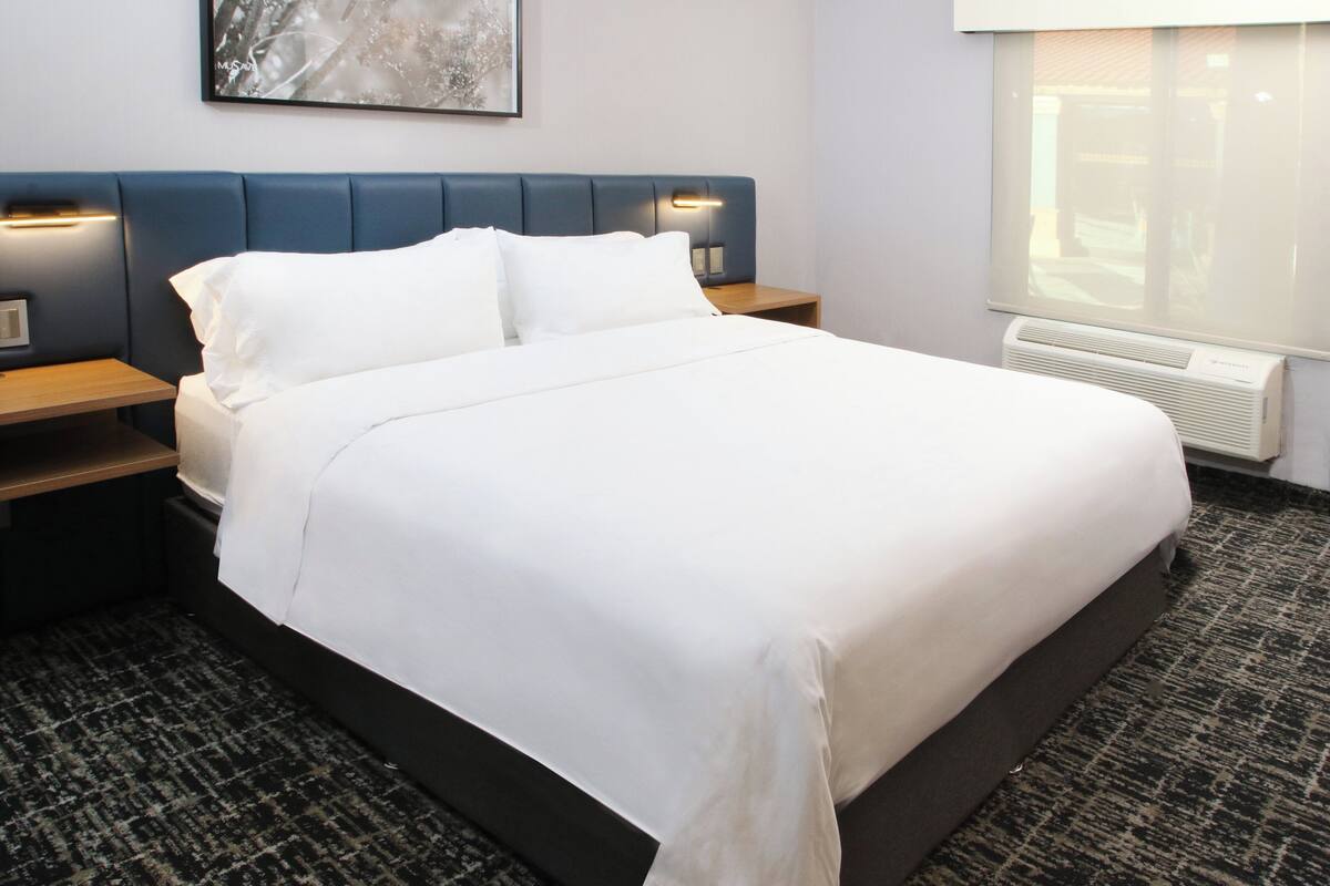 Cama bem arrumada com lençóis brancos, cabeceira azul e mesa de cabeceira com abajur.