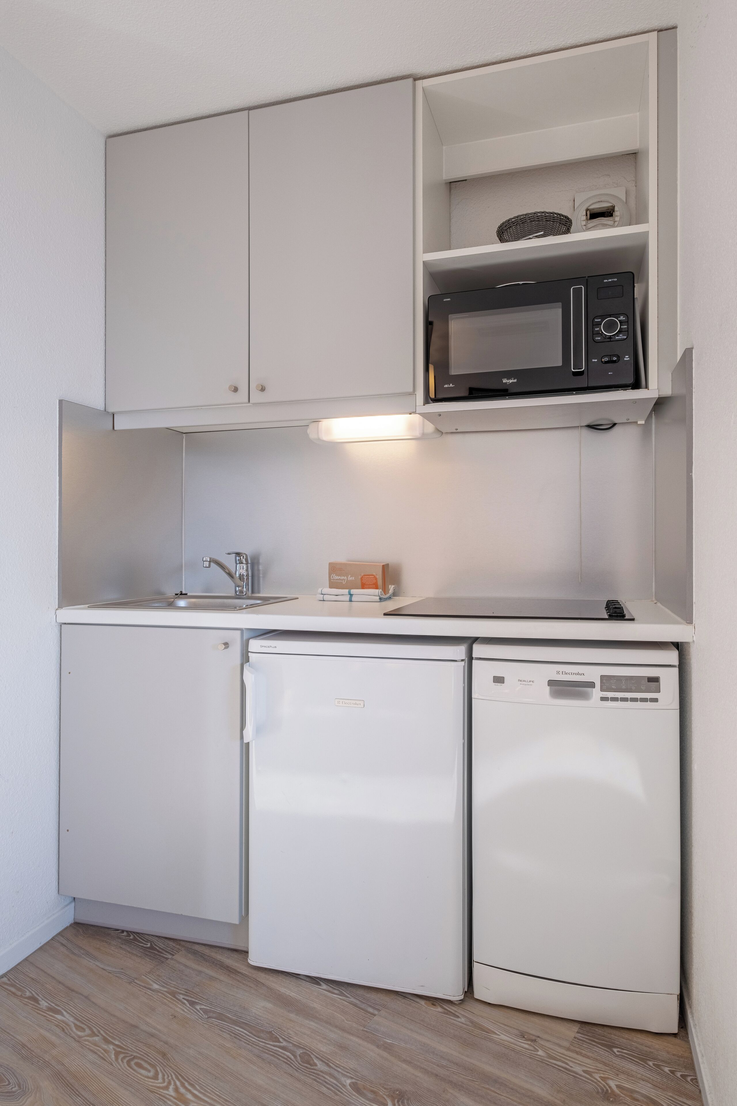 Cozinha compacta com armários brancos, micro-ondas, pia e máquina de lavar louça.