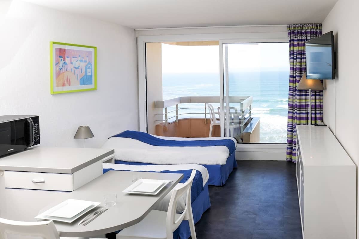 Quarto de hotel com cama, escrivaninha, cadeira, televisão e vista para o oceano.