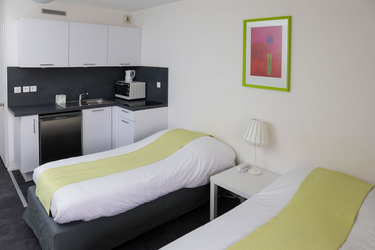 Quarto de hotel compacto com cozinha compacta, duas camas de solteiro, uma mesa de cabeceira e um criado-mudo.
