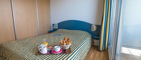Quarto de hotel com cama, mesa de cabeceira, janela com cortinas e vista para o exterior.