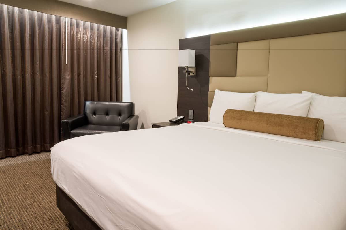 Quarto de hotel com uma cama grande, uma cadeira, uma mesa de cabeceira e uma televisão presa à parede.