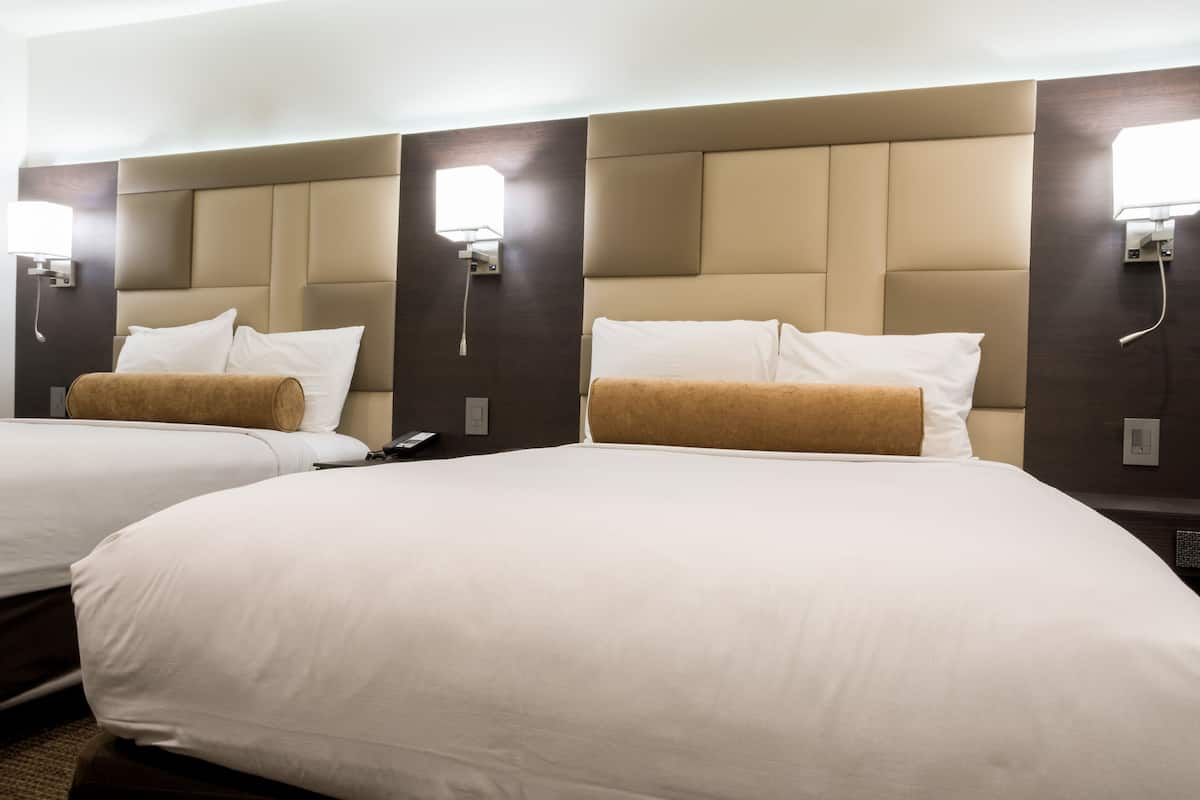 Quarto de hotel com duas camas, cada uma com roupa de cama branca e um cobertor marrom.