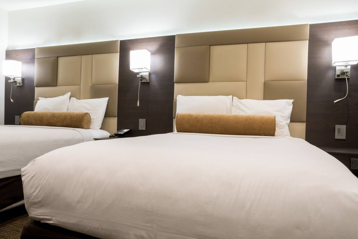 Quarto de hotel com duas camas, cada uma com cabeceira, roupa de cama branca e manta marrom.