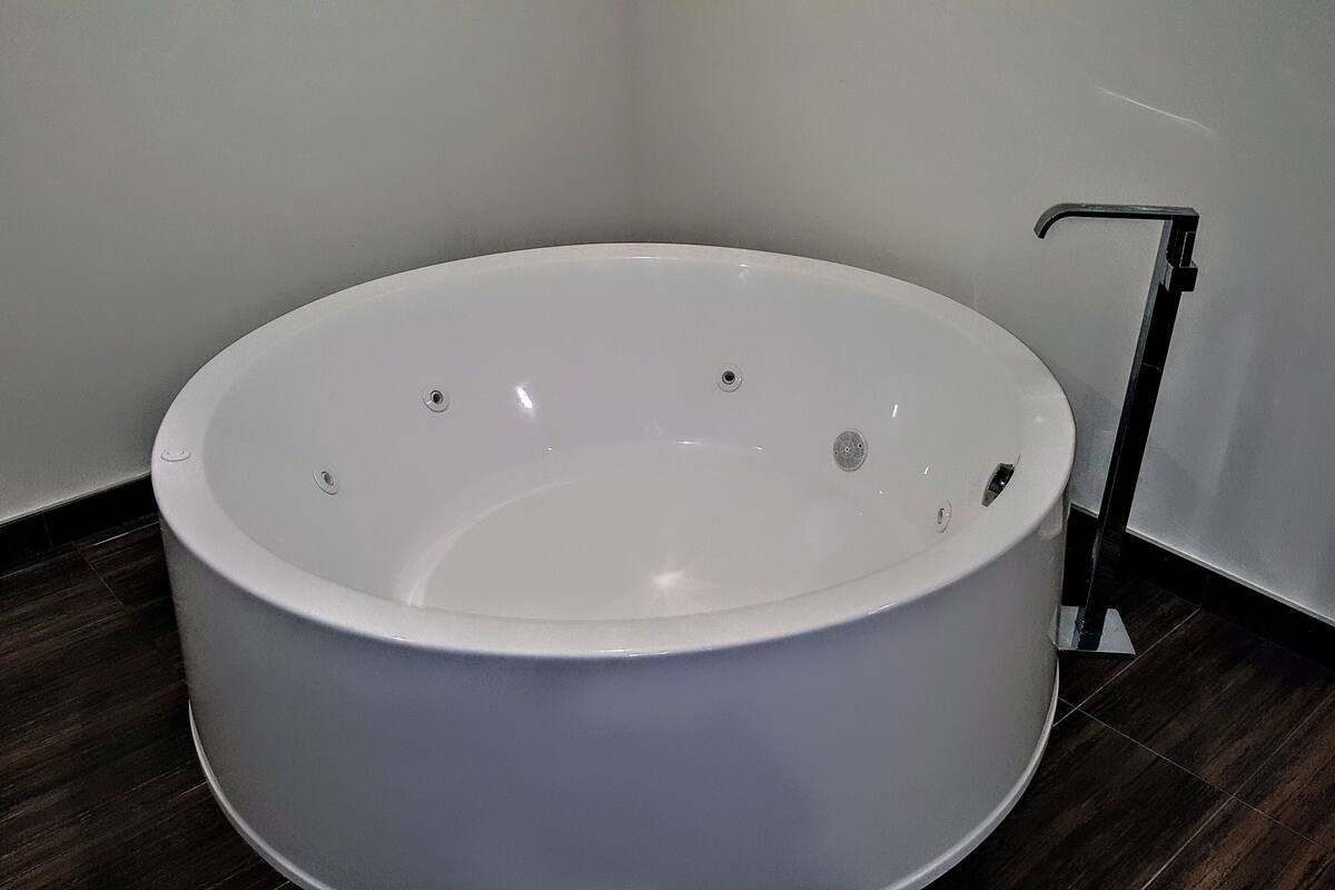 Um banheiro moderno com uma banheira grande e branca, piso de madeira escura e design minimalista.