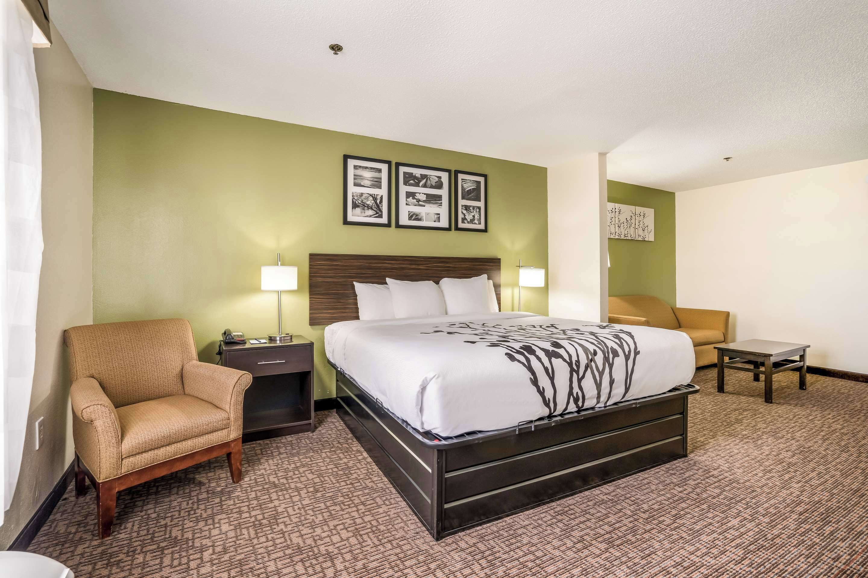 Quarto de hotel com uma cama grande, duas mesas de cabeceira, uma cadeira e uma mesinha.