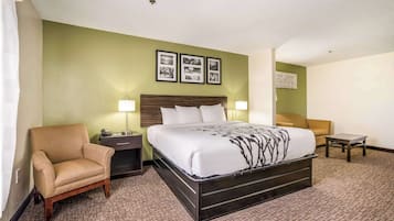Quarto de hotel com uma cama grande, duas mesas de cabeceira, uma cadeira e uma mesinha.
