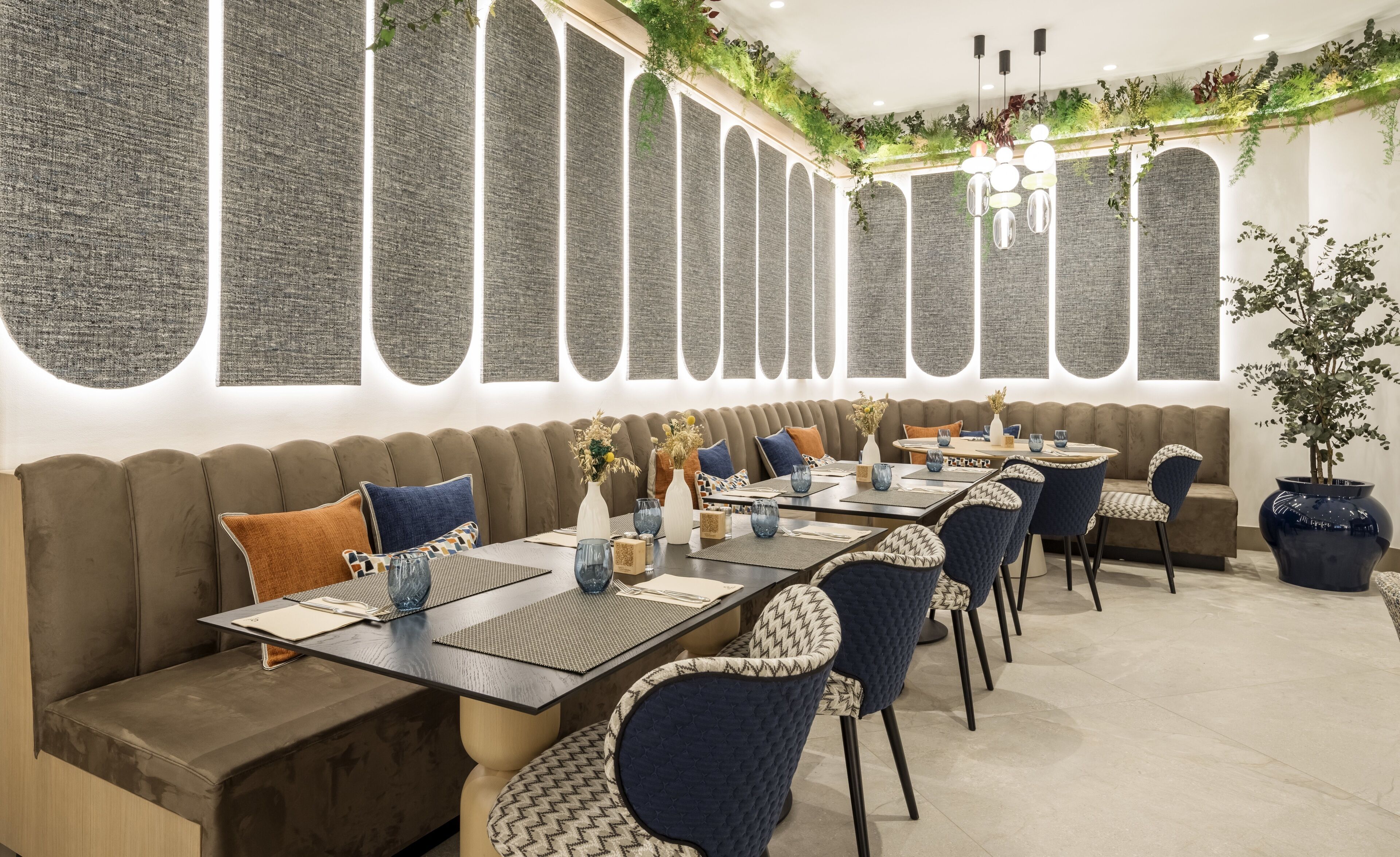 Um restaurante moderno com um amplo banco, mesas redondas e cadeiras azuis.