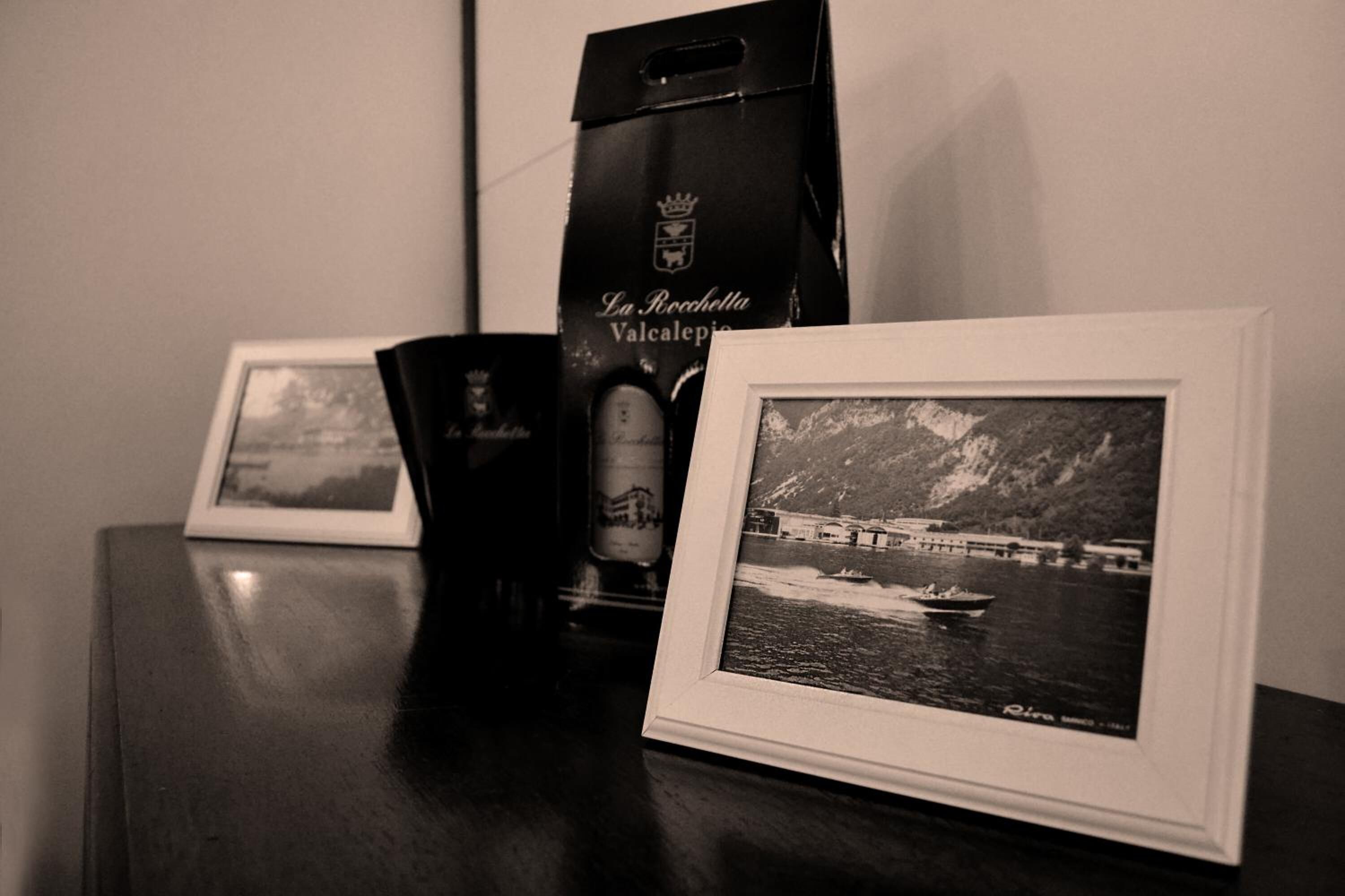 Uma fotografia emoldurada de uma paisagem costeira, uma garrafa de vinho e uma bolsa para vinho sobre uma mesa.