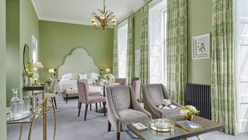 Quarto de hotel com uma cama, duas poltronas, uma mesa de jantar e um candelabro.