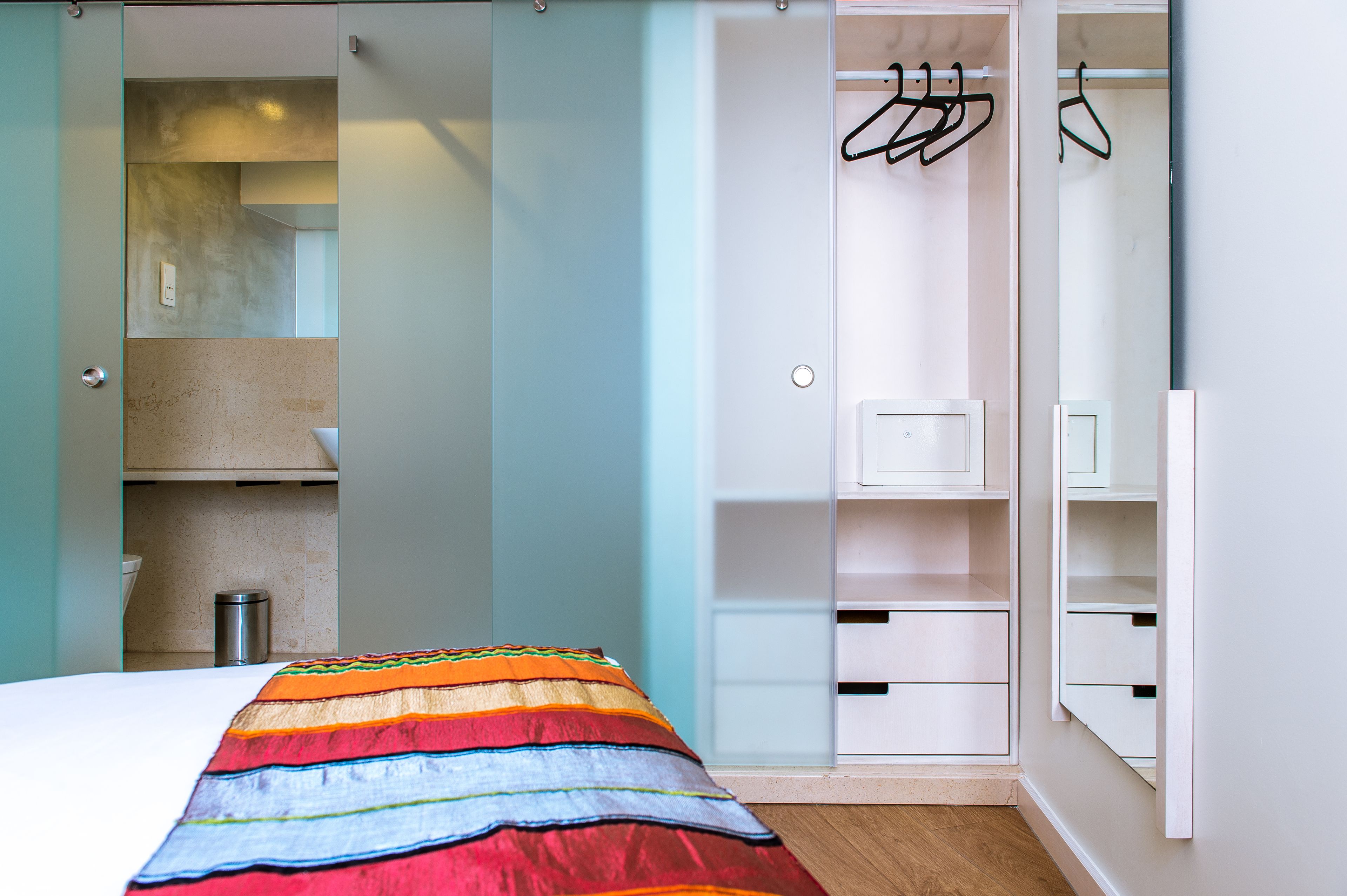 Quarto com cama, armário com espaço para pendurar roupas e uma pequena lixeira.