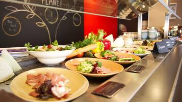 Buffet com diversos pratos, incluindo saladas e carnes, e uma lousa com a palavra 'PLANET' escrita.