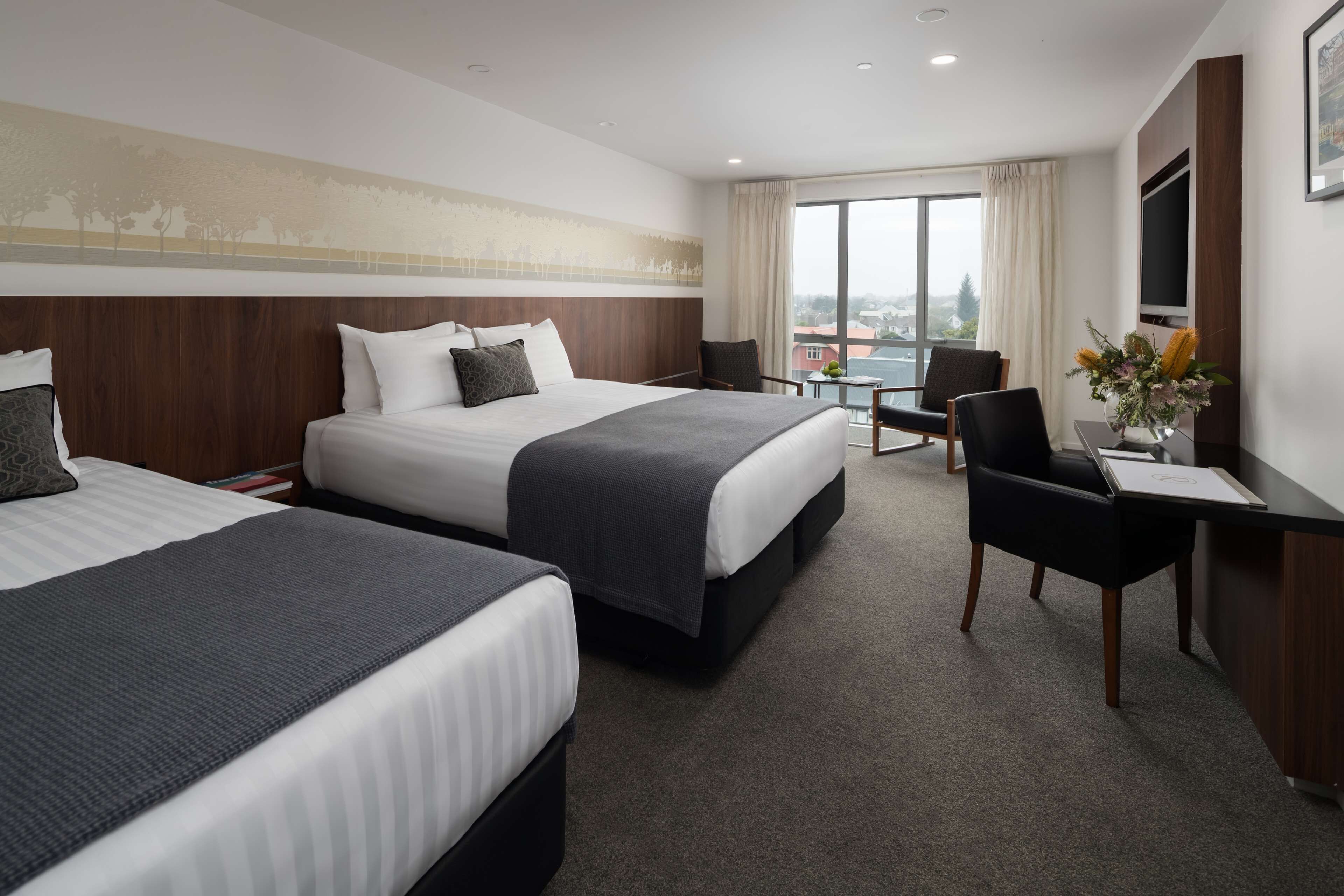 Quarto de hotel com duas camas, uma escrivaninha, uma cadeira e uma televisão.