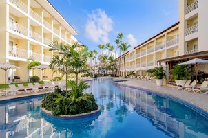 Um hotel com piscina, várias varandas e palmeiras.
