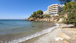 Hotel à beira-mar com várias varandas, uma costa rochosa e um céu azul límpido.