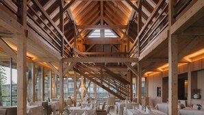Uma ampla sala de jantar com vigas de madeira altas e grandes janelas, proporcionando luz natural e vista para o exterior.