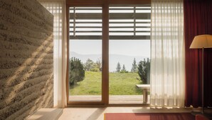 Quarto com uma grande porta de vidro deslizante que dá para uma área externa gramada, piso de madeira e tapete vermelho.