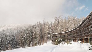 Um edifício moderno com fachada curva, rodeado por uma floresta coberta de neve.